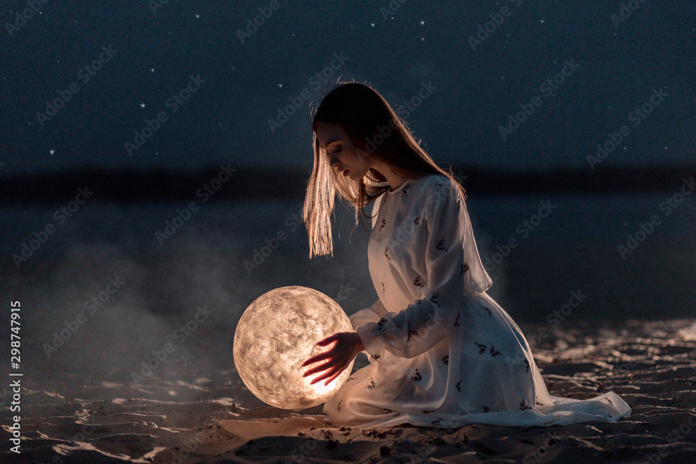 Beautiful young girl on a night beach with sand and stars holds the ...