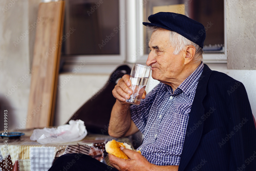 Senior old man pensioner drinking water while eating fast food burger ...