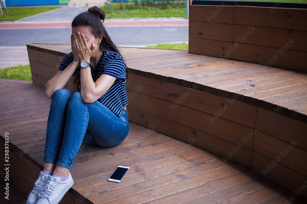 Girl crying, covering face with hands, sitting with legs on a wooden ...