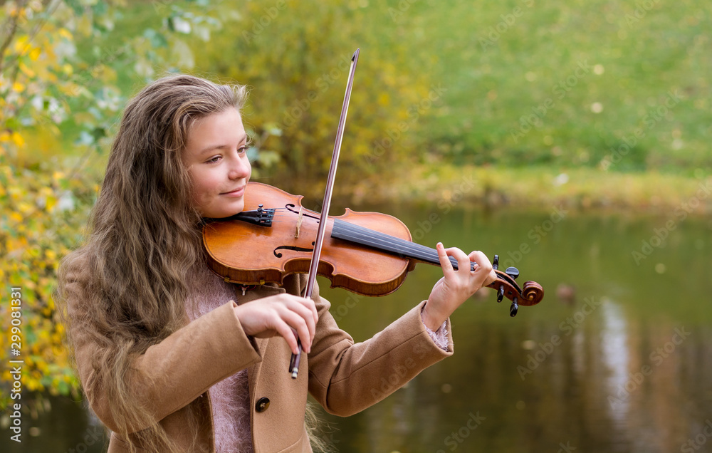 Girl playing the violin and smiling in the autumn park at a lake ...