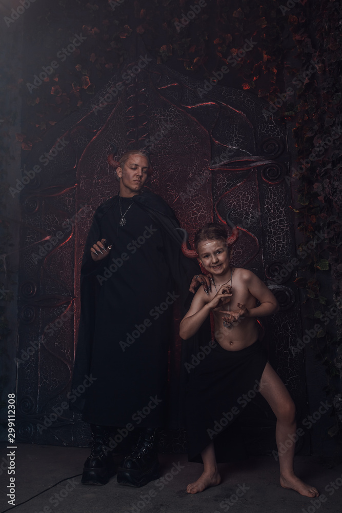 small child with red horns of demon and adult scary man standing in ...