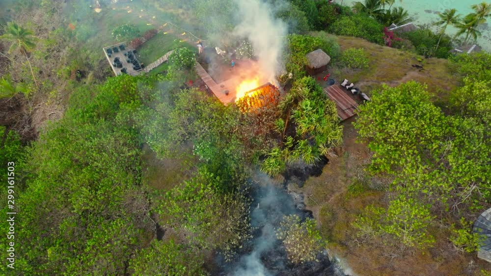Aerial of a straw hut burning on a beautiful tropical island, Fireman ...