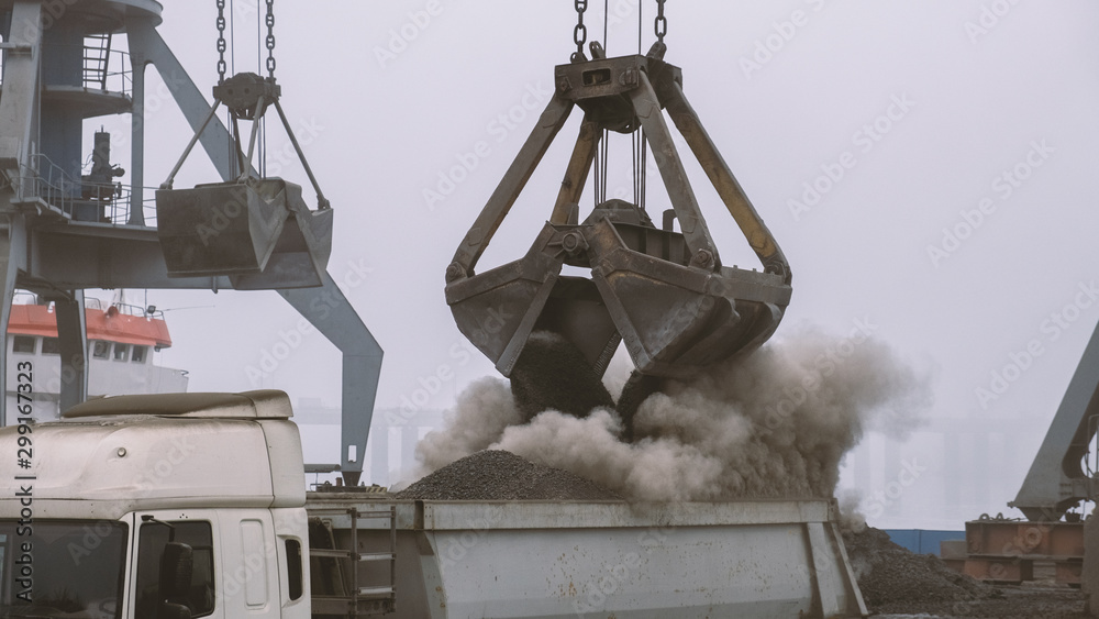 Grapple crane unloading cement clinker from ship to truck in river port ...