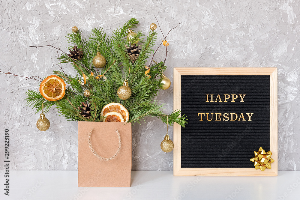 Happy Tuesday text on black letter board and festive bouquet of fir ...