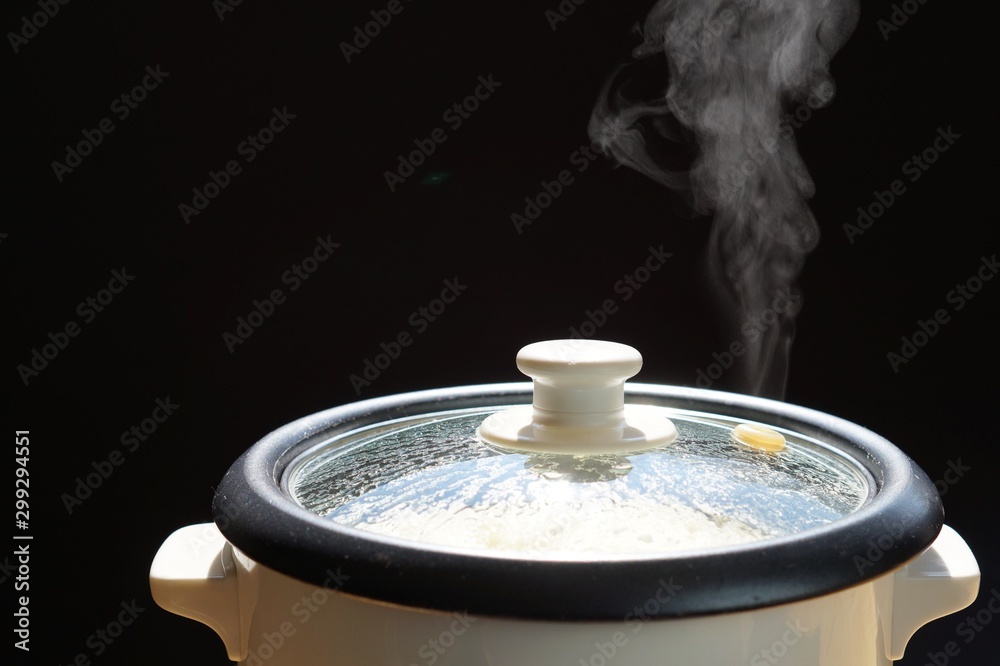 hot cooked rice in electric rice cooker with steaming on dark ...