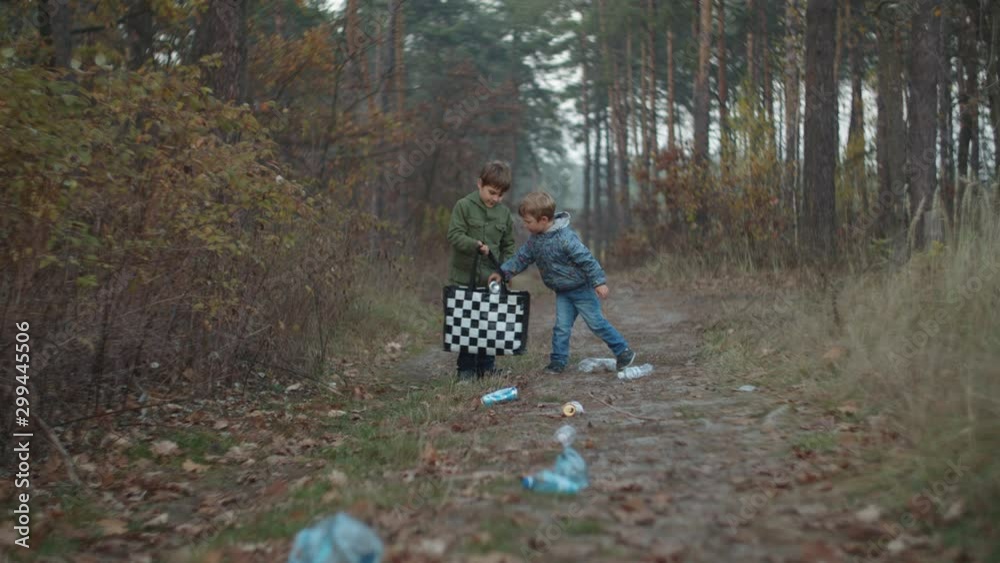 Two boys in jackets collecting plastic waste in fall park on sunset in ...