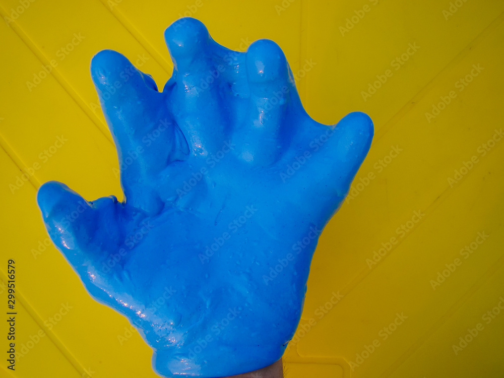 Molten blue plastic wraps around a hand. Yellow background ...