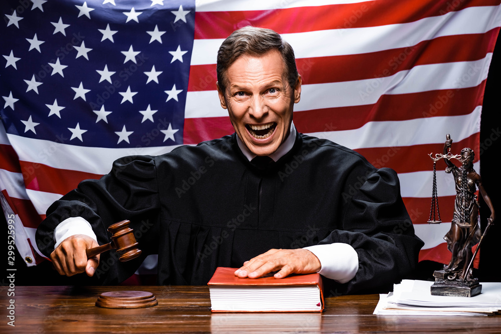 angry judge in judicial robe hitting gavel and putting hand on book ...