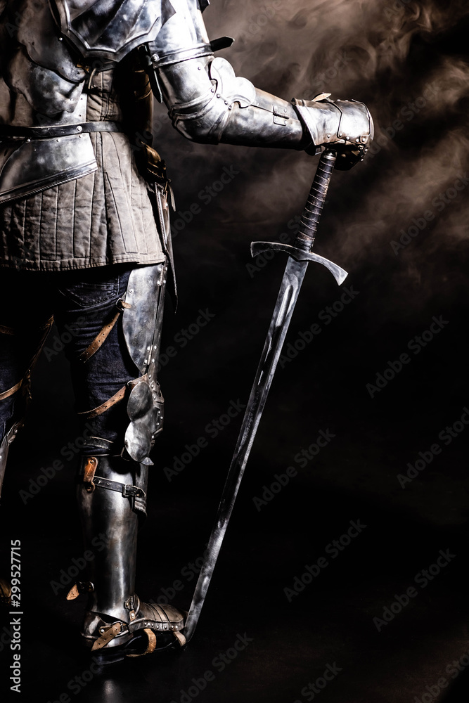 cropped view of knight in armor holding sword on black background Stock ...