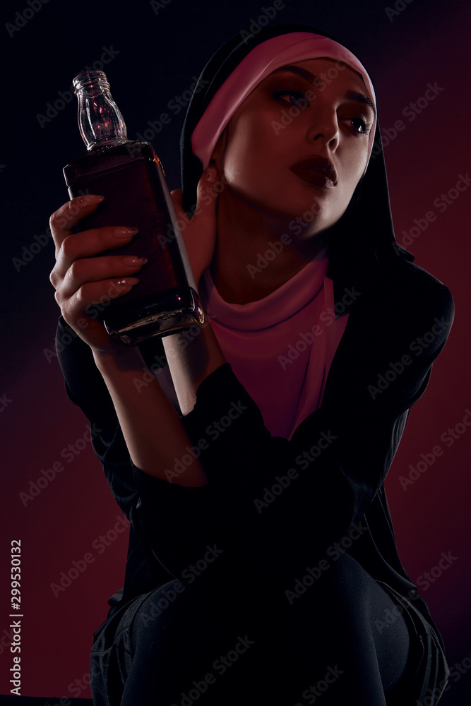 Cropped shot of a nun, sitting on a dark burgundy background. She ...