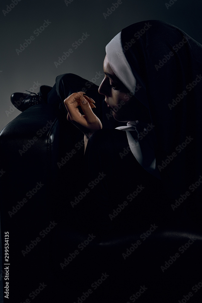 Upward half-turn back view shot of a nun, sitting on a chair. She's ...