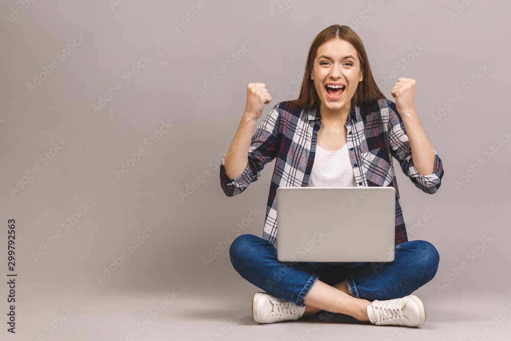 Winner! Excited smiling girl sitting on floor with laptop, raising one ...