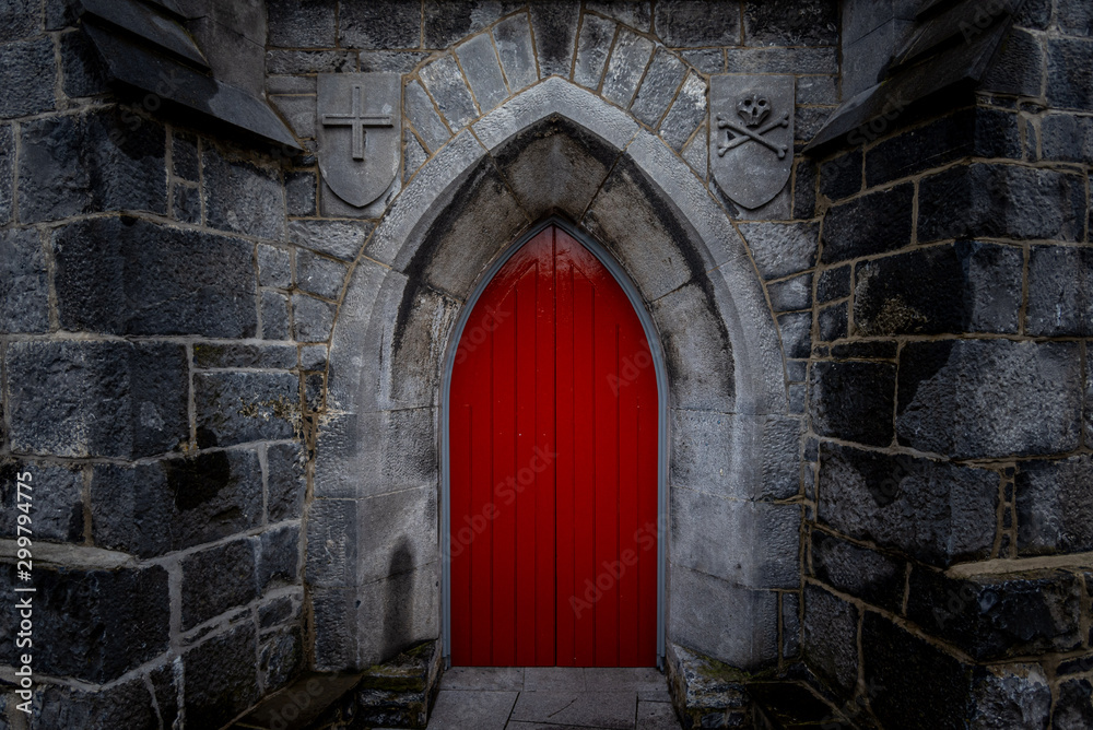 Scary pointy red wooden door in an old and wet stone wall building with ...