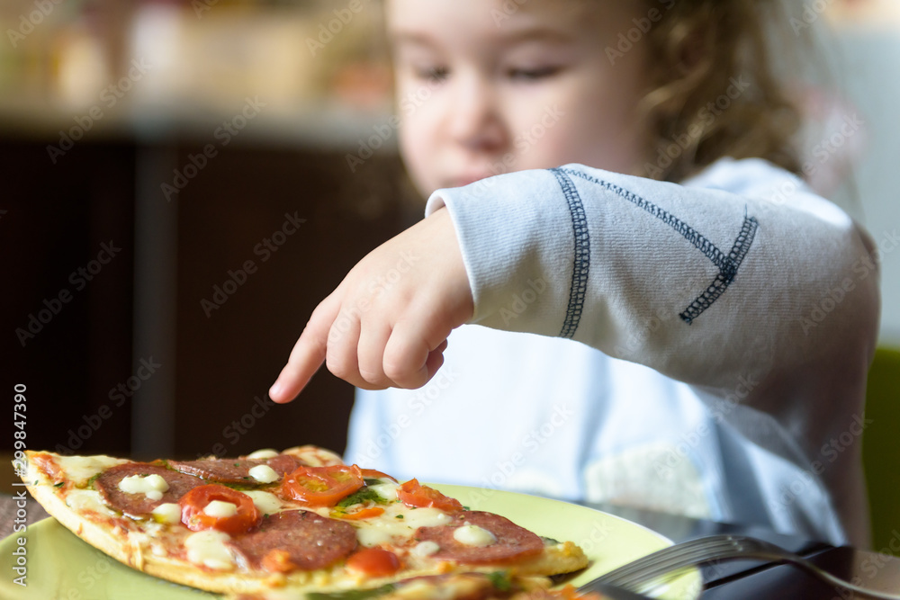 Child looks and points a finger at pizza on table. Three years old kid ...