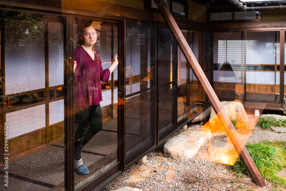 Japan with young woman standing looking through window sliding door on ...