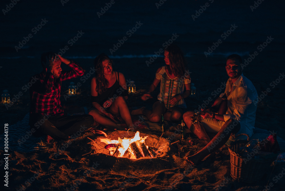 Circle of campers around campfire sitting on the beach near the sea ...
