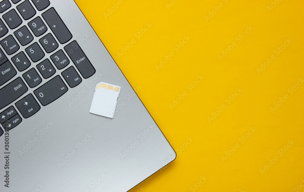 Laptop and SD memory card on yellow paper background. Modern gadgets ...