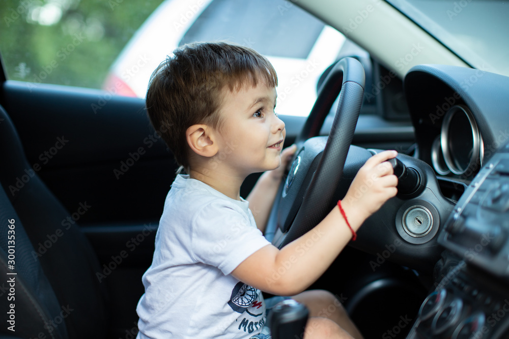 Little boy sitting behind the wheel of a car with a lovely smile on his ...