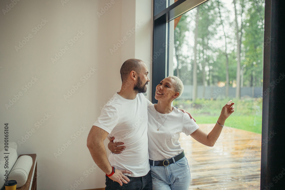 Lovely couple in white clothes look at window with view on garden ...