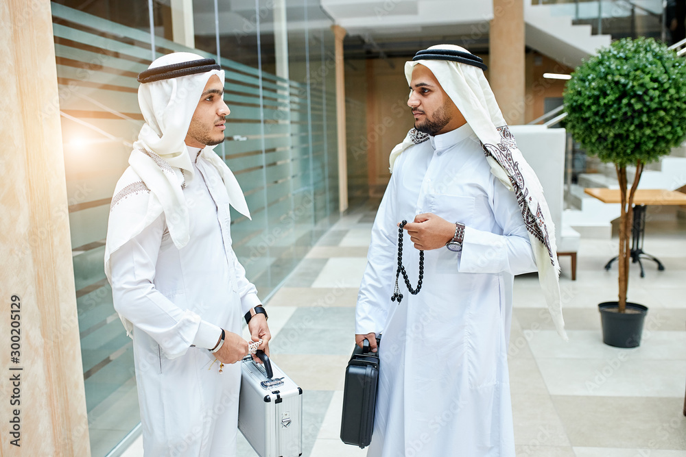 Two arabic men with cases speak, talk. In white suits. Business center ...