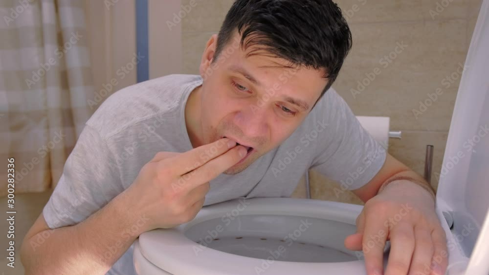 Portrait of man is vomiting in toilet sitting on the floor with two ...