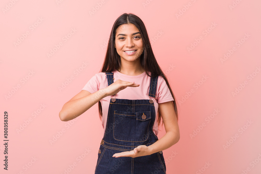 Young pretty arab woman wearing a jeans dungaree holding something with ...