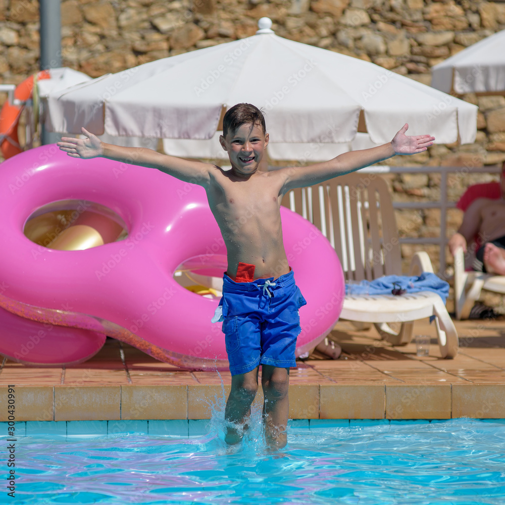Caucasian boy in blue swimming shorts jumping into swimming at resort ...