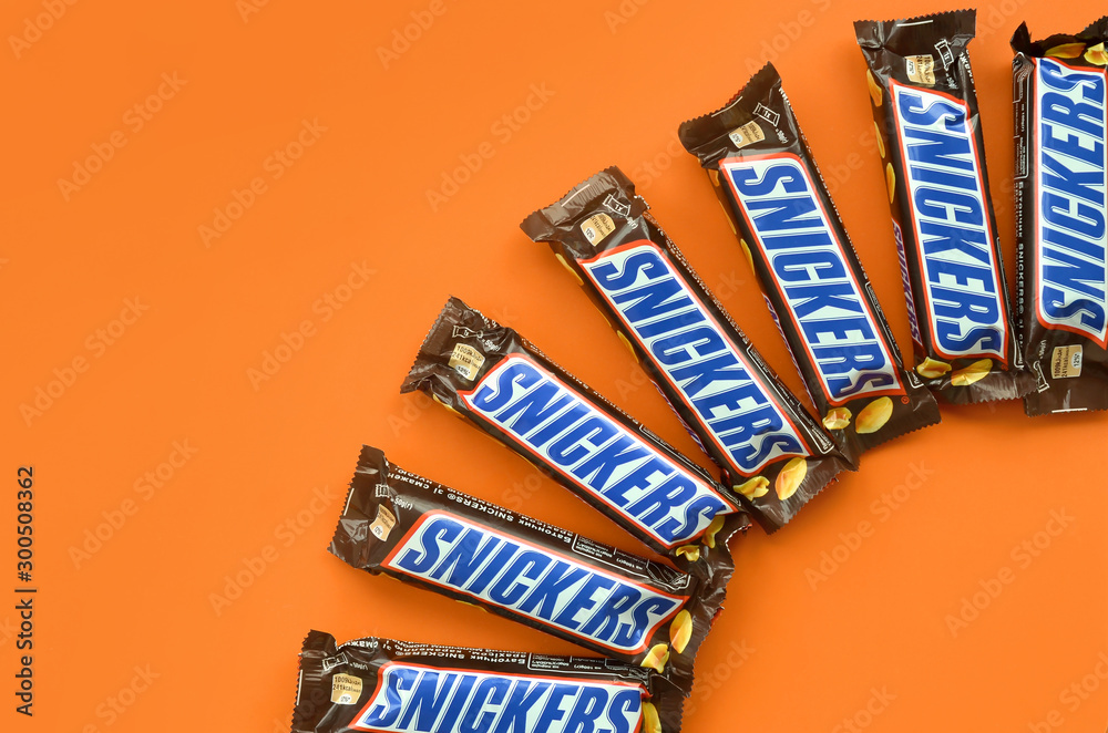 Many Snickers chocolate bars lies on pastel orange paper. Snickers bars ...
