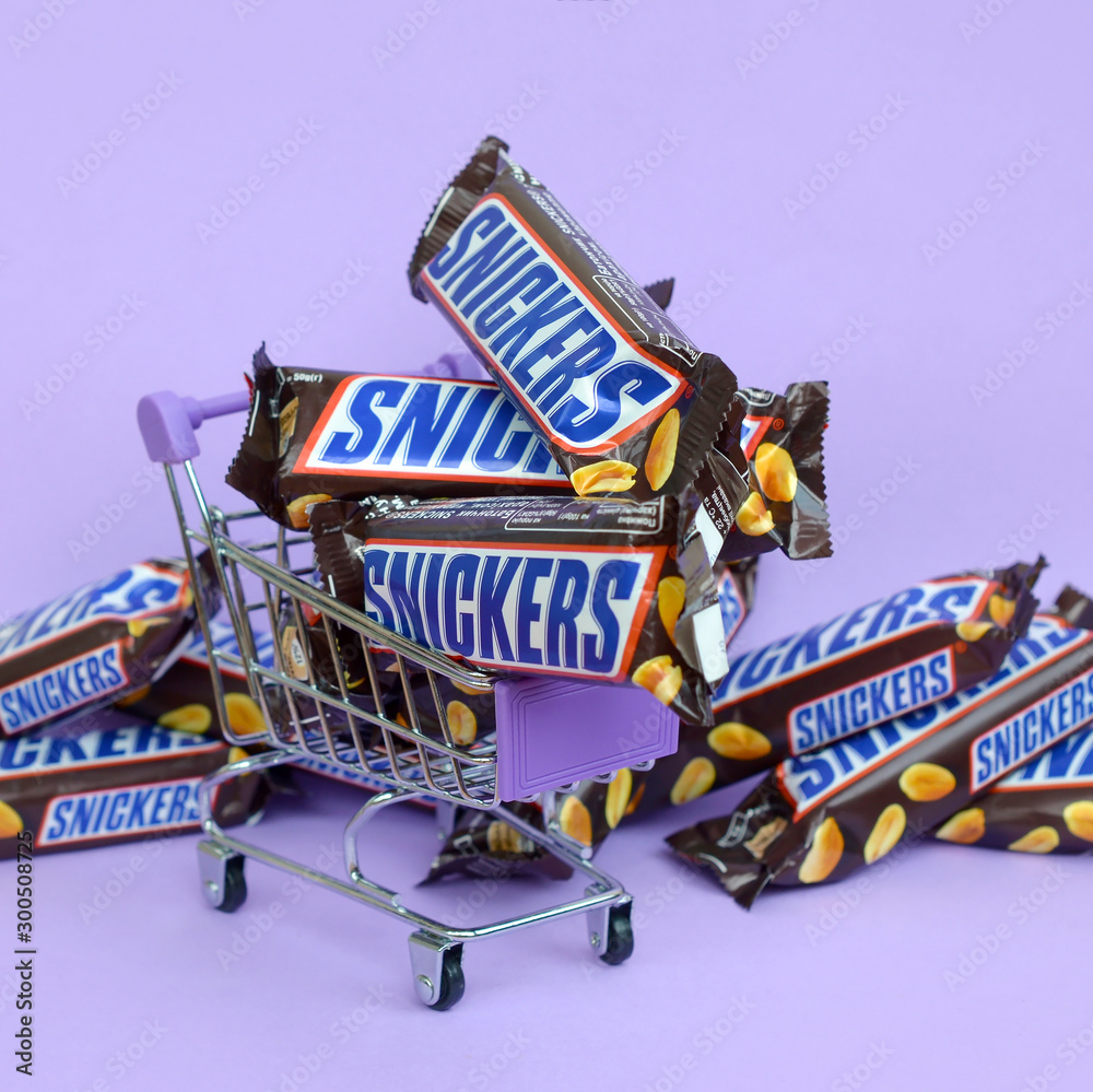 Many Snickers chocolate bars stacked close up with shopping cart on ...