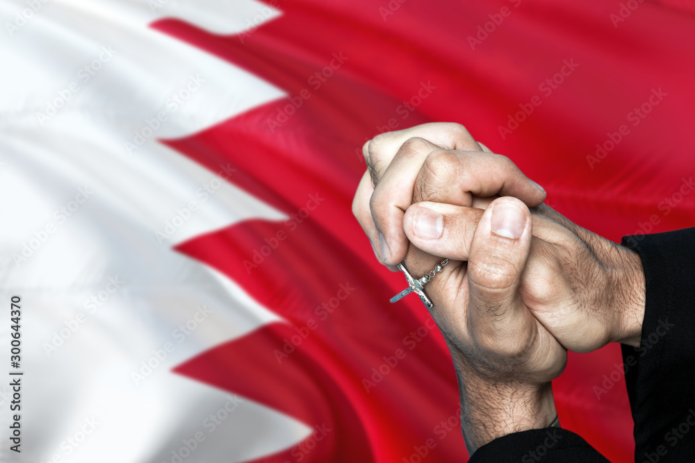 Bahrain flag and praying patriot man with crossed hands. Holding cross ...
