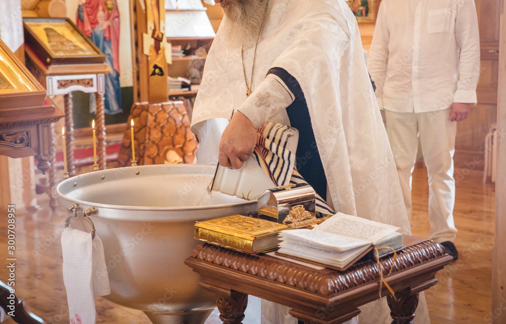 Christening ceremony in the Orthodox church, priest lighting candles at children baptismal font ...