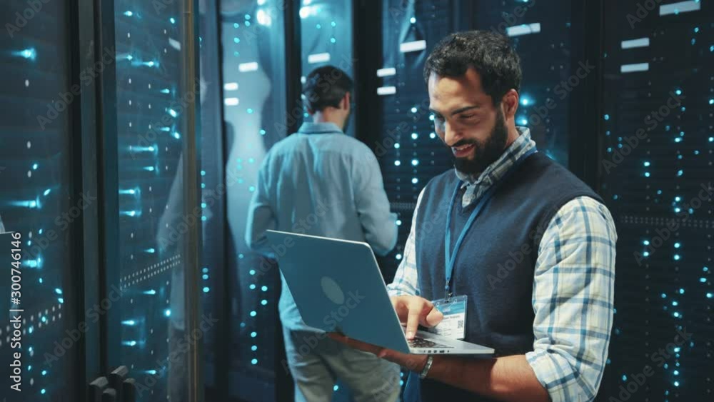 Cheerful IT administrator checking network servers on rack typing data ...