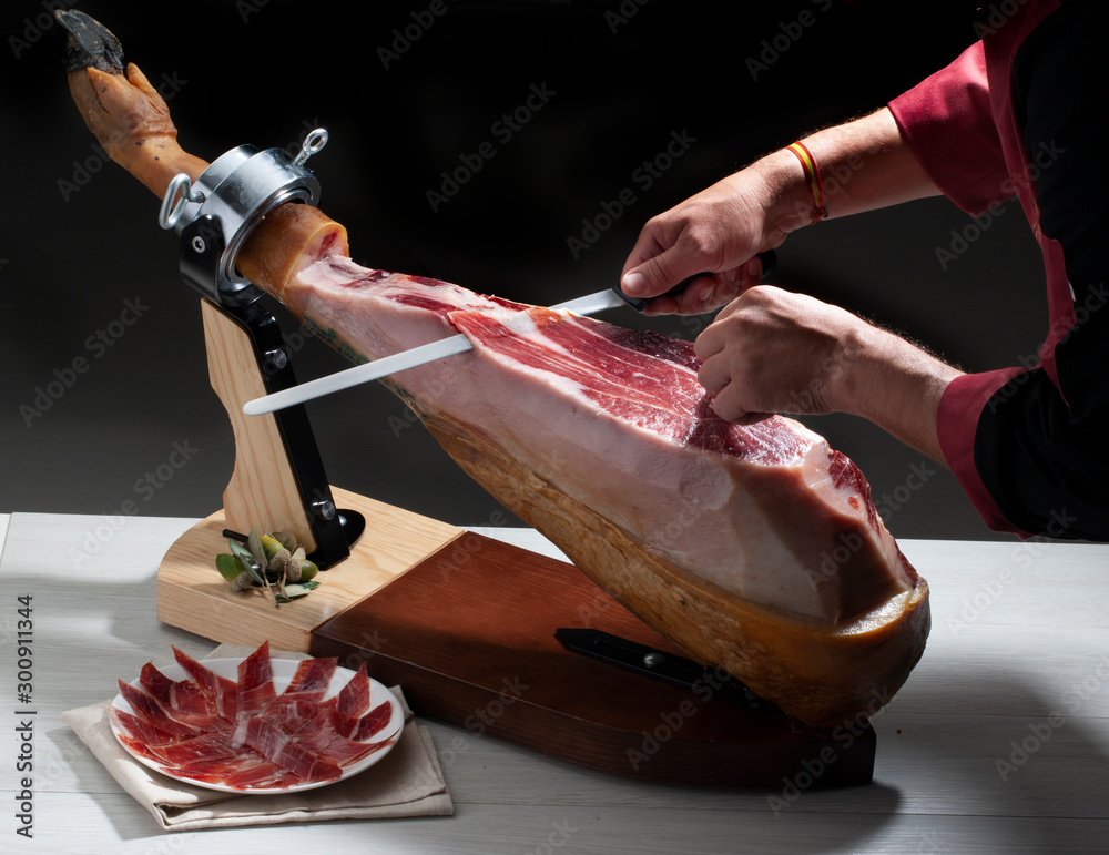 Mano cortando jamón y plato de jamón . Hand cutting ham and plate of ...