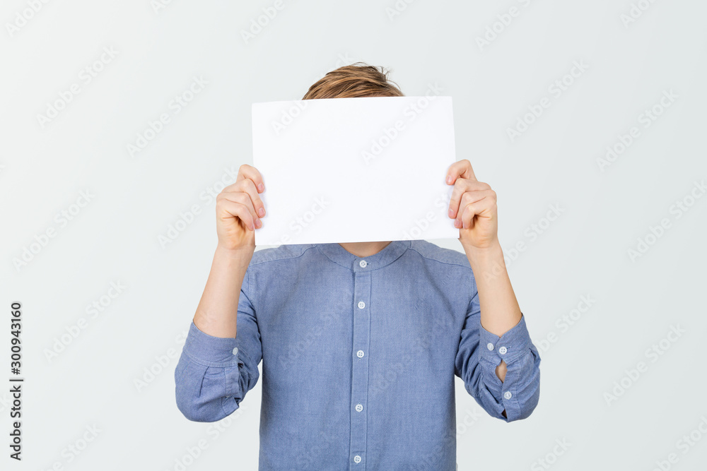 Teenage boy covering his face with a empty white paperT over white ...