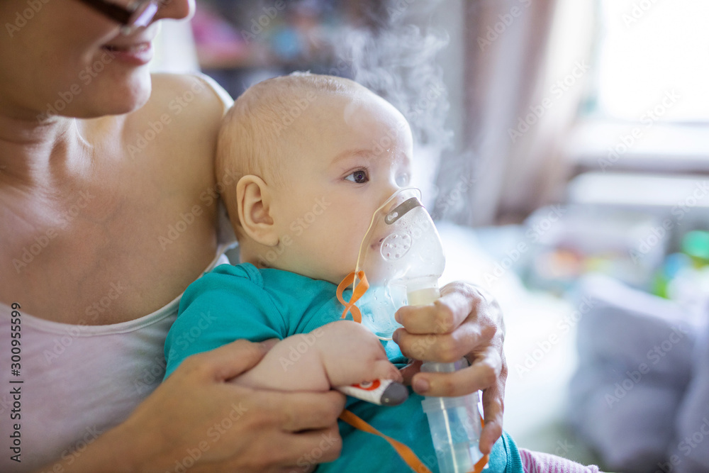 Baby girl making inhalation with nebulizer while sitting on mom's lap ...