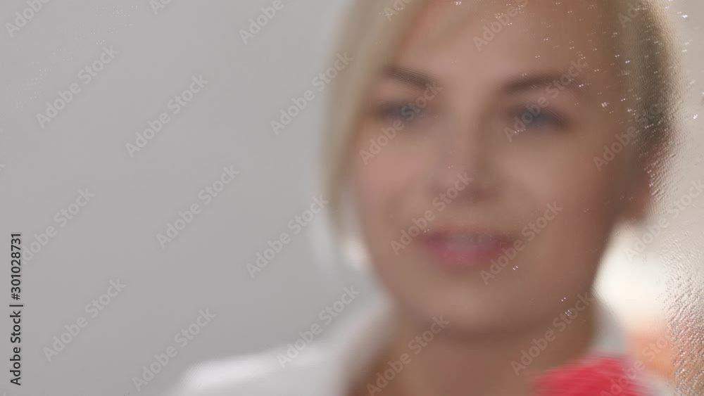 Close-up reflection of lovely cleaning lady appearing on mirror surface ...