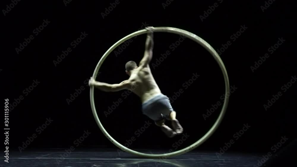 Muscular circus artist in the Cyr Wheel doing difficult tricks slow ...