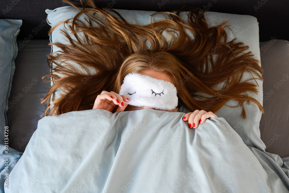Young woman with long hair and a red manicure is sleeping in bed with ...