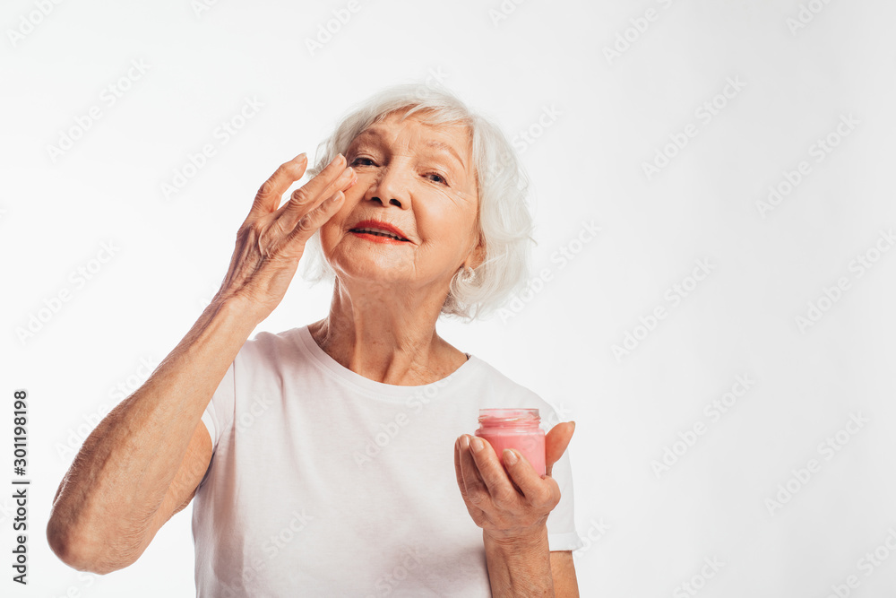 Process of old woman hold pink jar of face cream in one hand and put ...