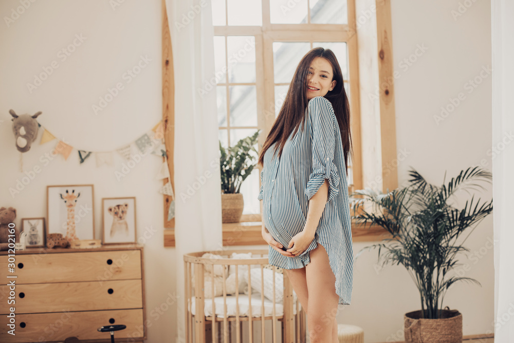 Excited young pregnant woman stand in room and posing on camera. Hold ...