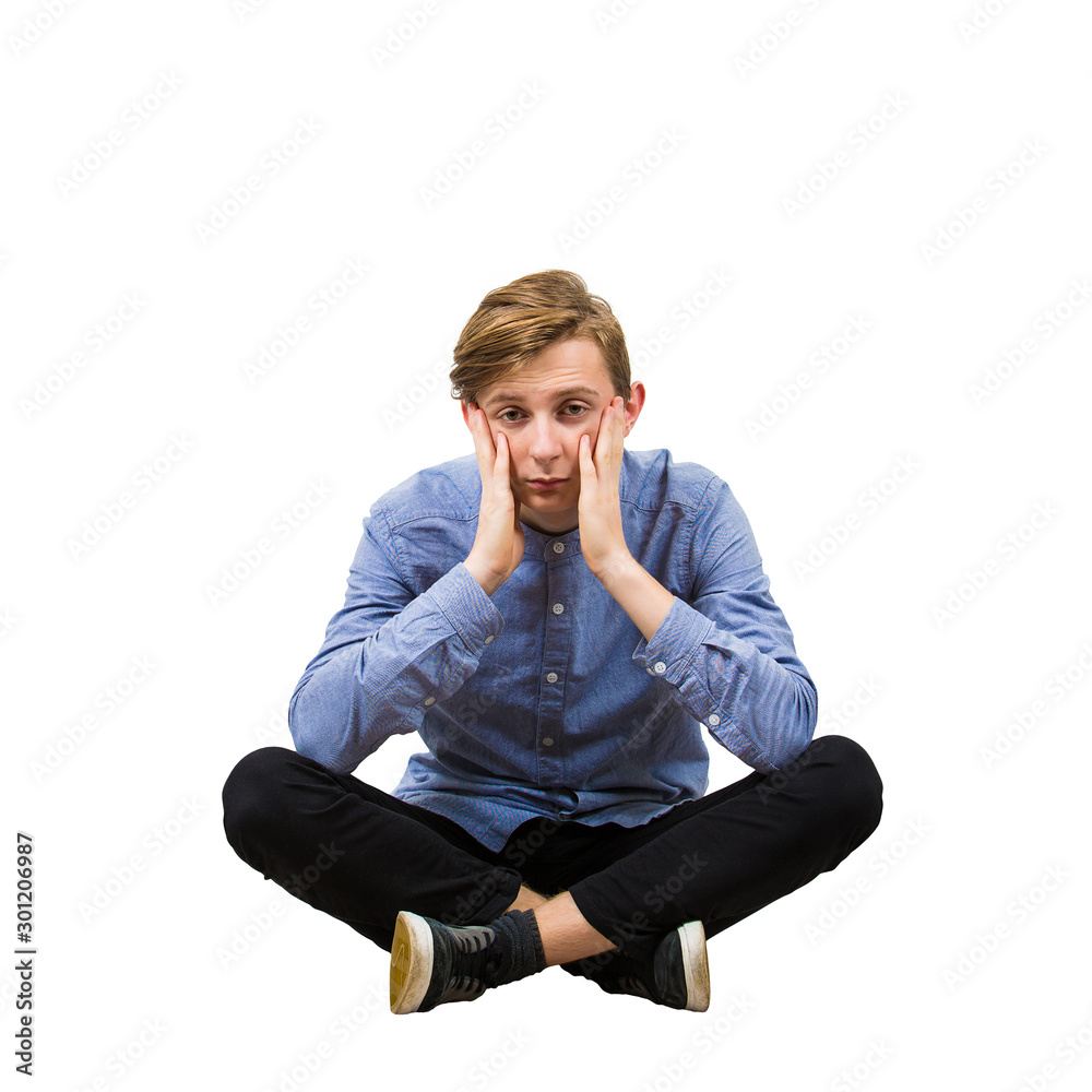 Upset and stressed teenage guy seated on the floor with crossed legs ...