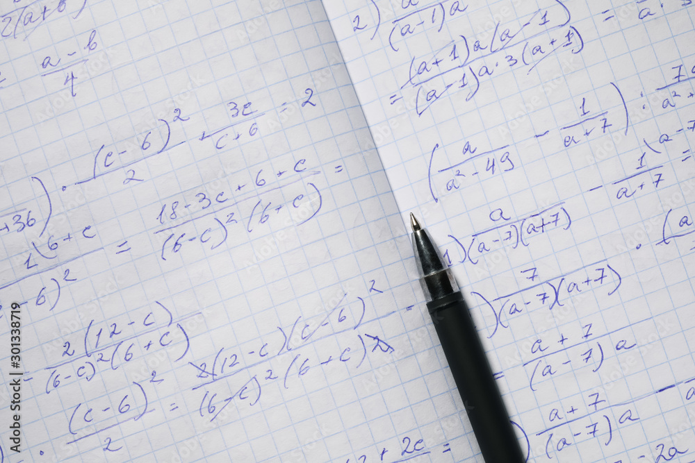Algebraic calculations in open graph notebook with black pen. White ...