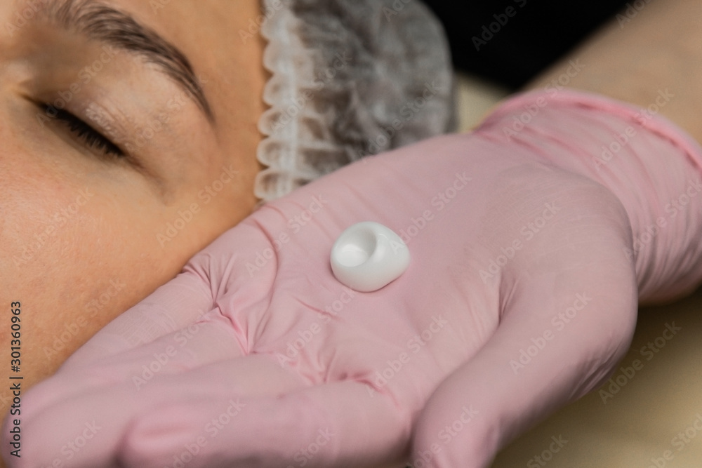 concept beautician. The hands of a cosmetologist put cream on the face ...