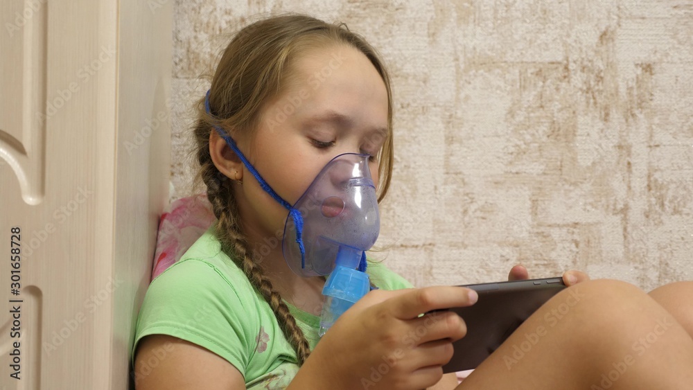 child with a tablet is sick and breathes through an inhaler. close-up ...