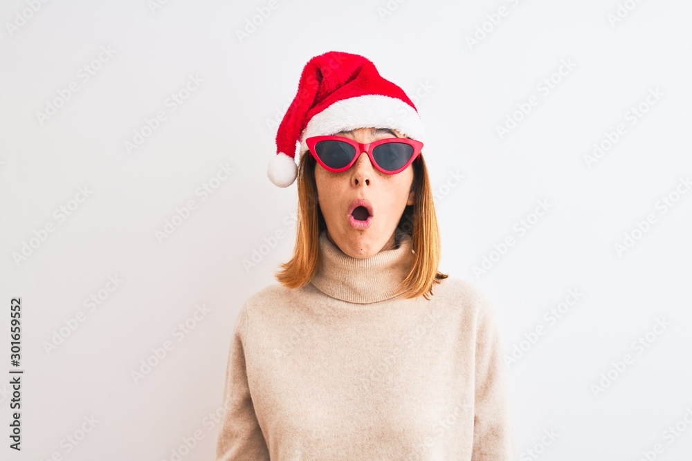 Beautiful redhead woman wearing christmas hat and red sunglasses scared ...