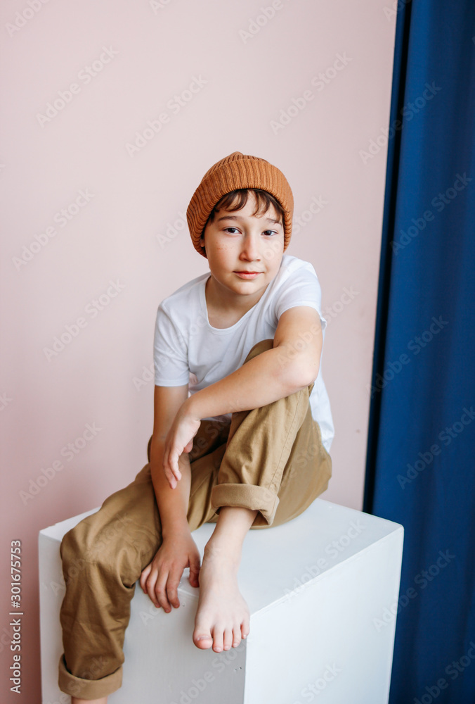 Fashionable attractive tween boy with dark hair in hat sitting on white ...