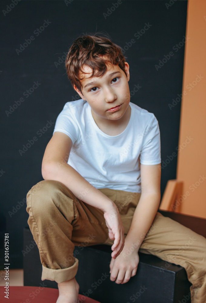 Fashionable attractive tween boy with dark hair stting on black cube in ...