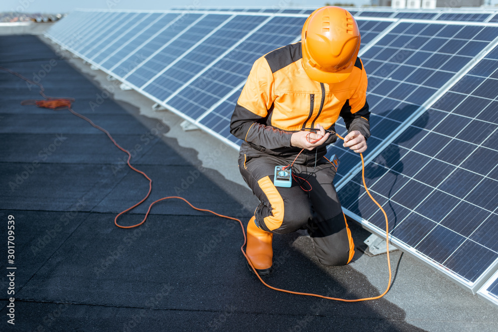 Well-equipped electrician connecting solar panels, checking the voltage ...