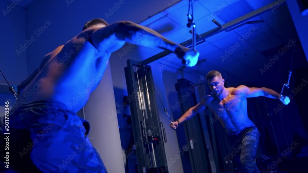 Shirtless bodybuilder during workout in blue light. Reflection in a ...