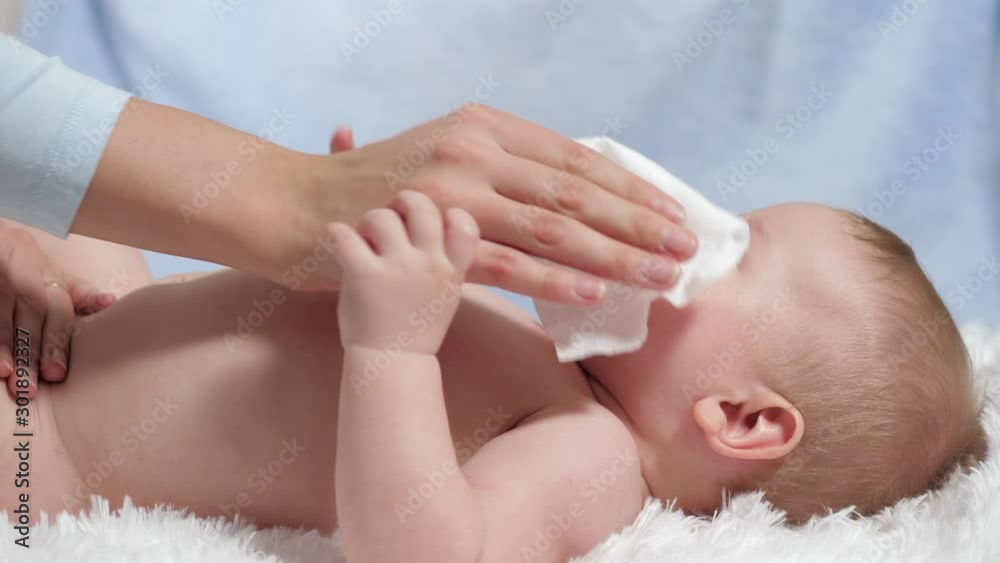 Mom wipes baby with wet wipe. Child lies on white blanket on blue ...